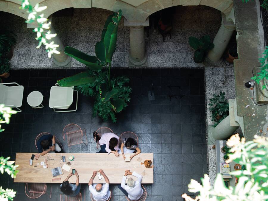 Uma área de estar externa com uma mesa comprida, cadeiras e plantas em vasos.