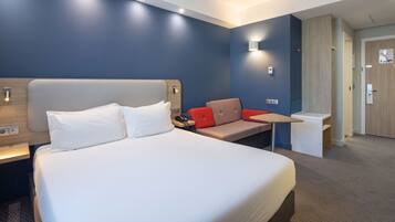 Quarto de hotel com uma cama grande, uma escrivaninha, uma cadeira e uma pequena mesa.