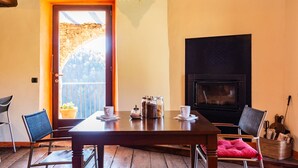 Um quarto acolhedor com uma mesa de madeira, cadeiras, lareira e vista para uma parede de pedra através de uma porta.