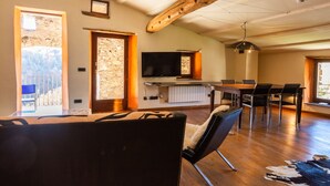 Uma sala de estar ampla com teto de madeira, uma mesa de jantar com cadeiras, uma televisão de tela plana e uma parede de pedra.