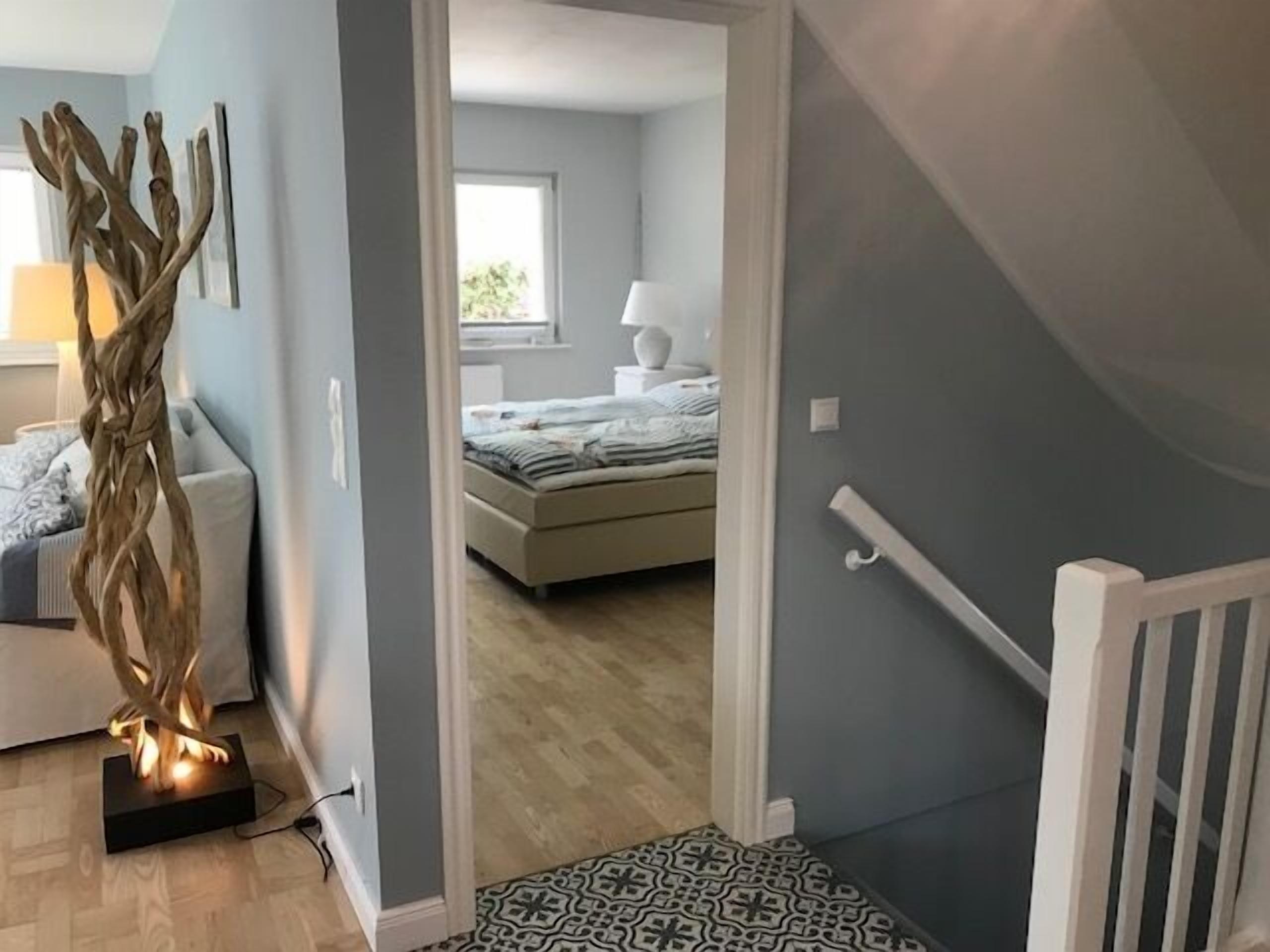 Quarto moderno com cama, mesa de cabeceira e escultura decorativa de árvore.