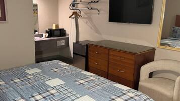 Quarto com cama, penteadeira, cadeira e televisão fixada na parede.