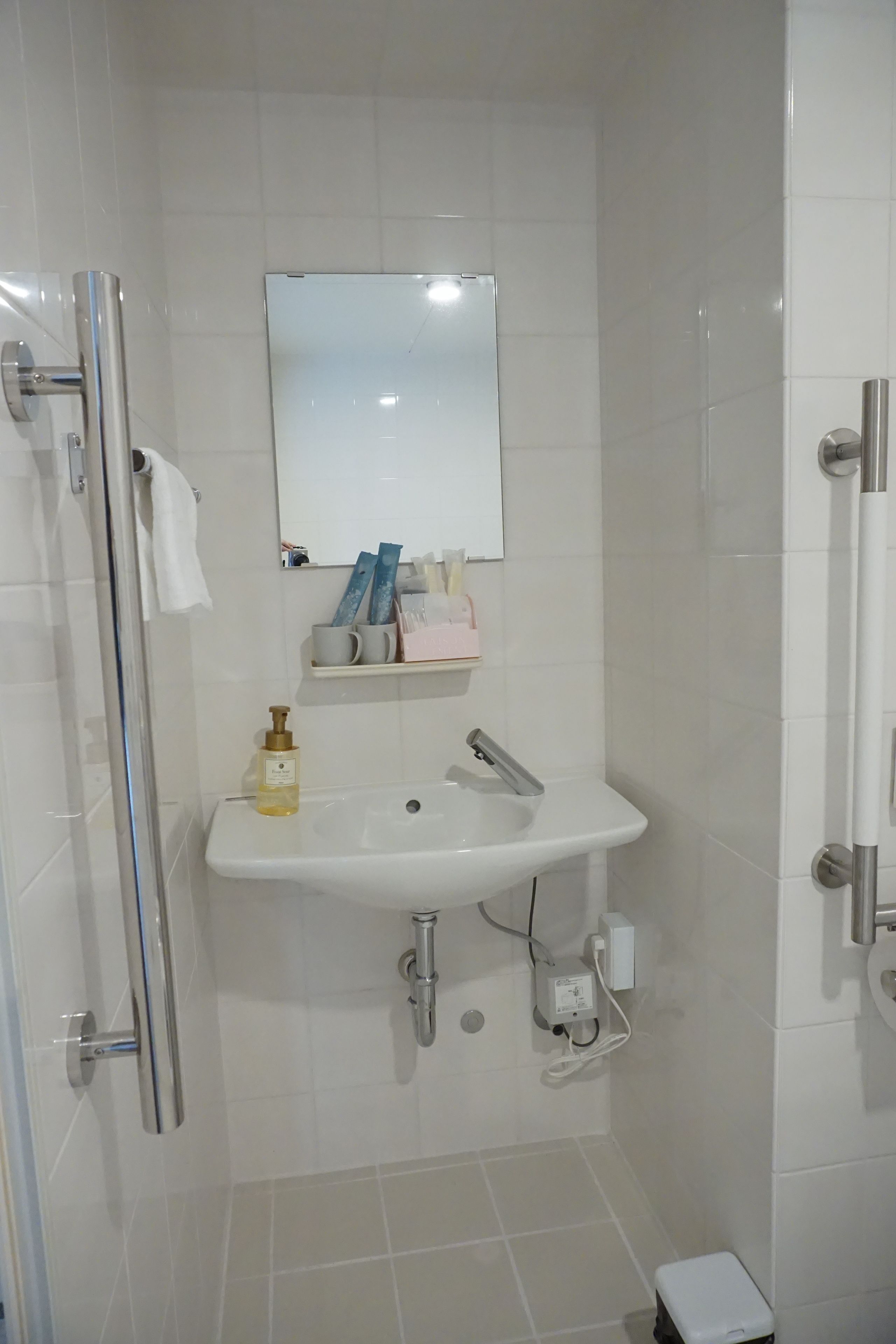 Casa de banho com lavatório branco, espelho e área de duche.