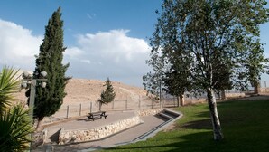 Um parque com um banco de pedra, uma mesa para piquenique e uma área cercada com árvores.