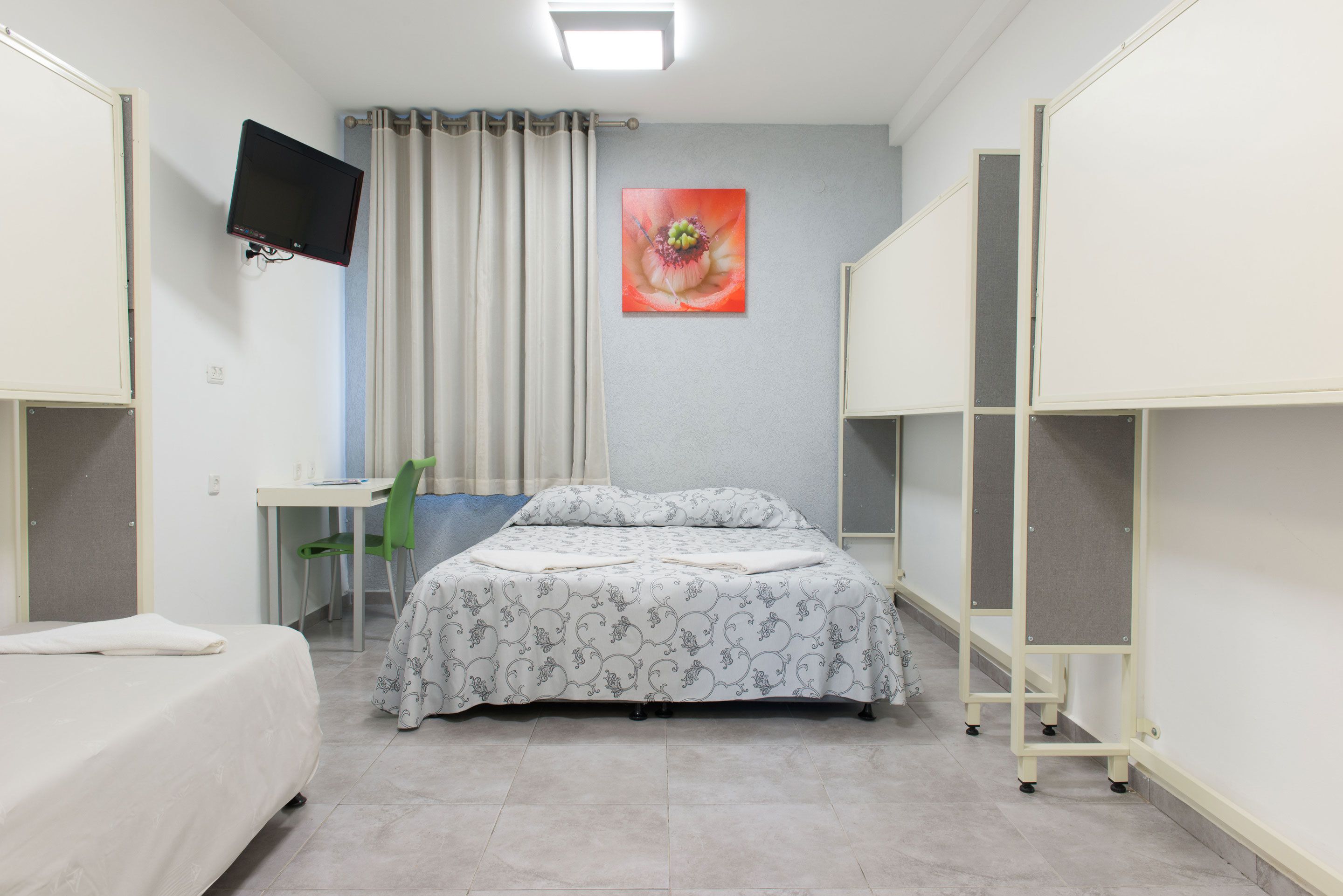 Quarto com cama, escrivaninha, cadeira, televisão e armários.