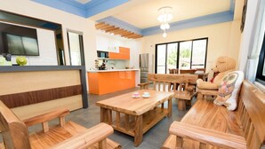 Uma sala de estar moderna com móveis de madeira, uma cozinha ao fundo e uma janela grande.