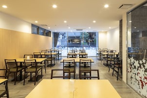 Restaurante com várias mesas e cadeiras, parede de madeira e uma grande janela com vista para um edifício.