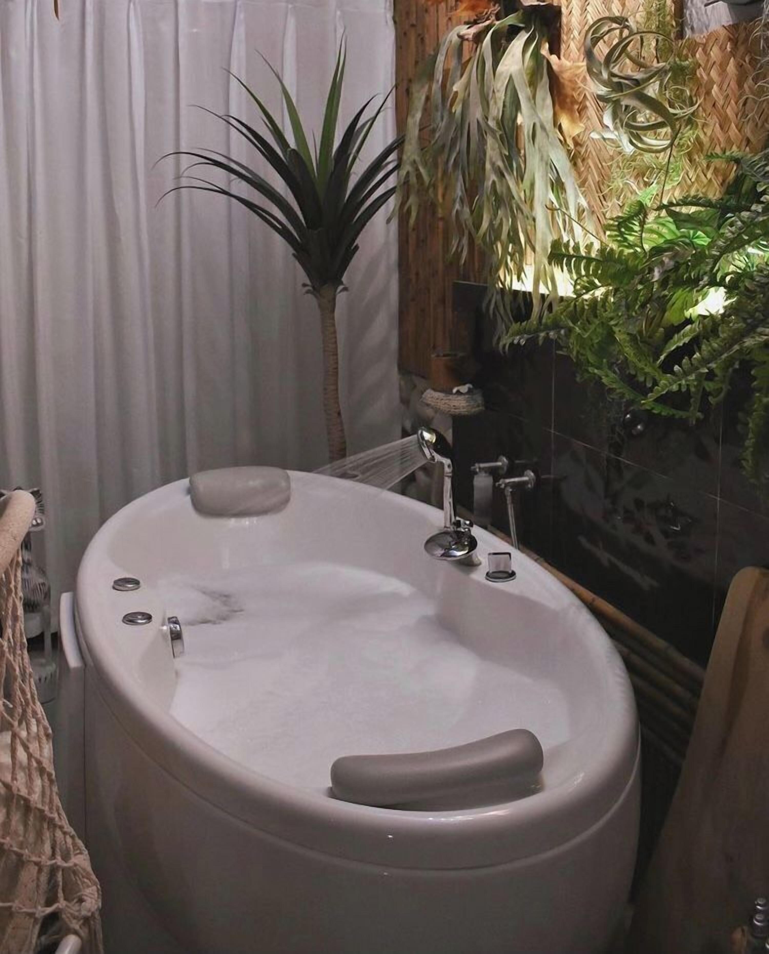 Um banheiro com banheira independente, uma planta em vaso e um detalhe decorativo na parede.