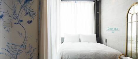 Quarto com cama, cortinas brancas, janela e parede com padrão floral azul.