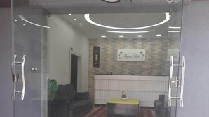 Um saguão de hotel com uma mesa de recepção, um sofá e uma mesa de centro. Há degraus que levam a uma porta de vidro.