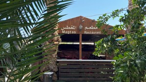 Um restaurante chamado 'Magtas', com fachada de madeira e letreiros em árabe e inglês.