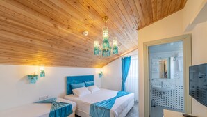 Quarto com duas camas, teto de madeira, lustre e banheiro com pia e espelho.