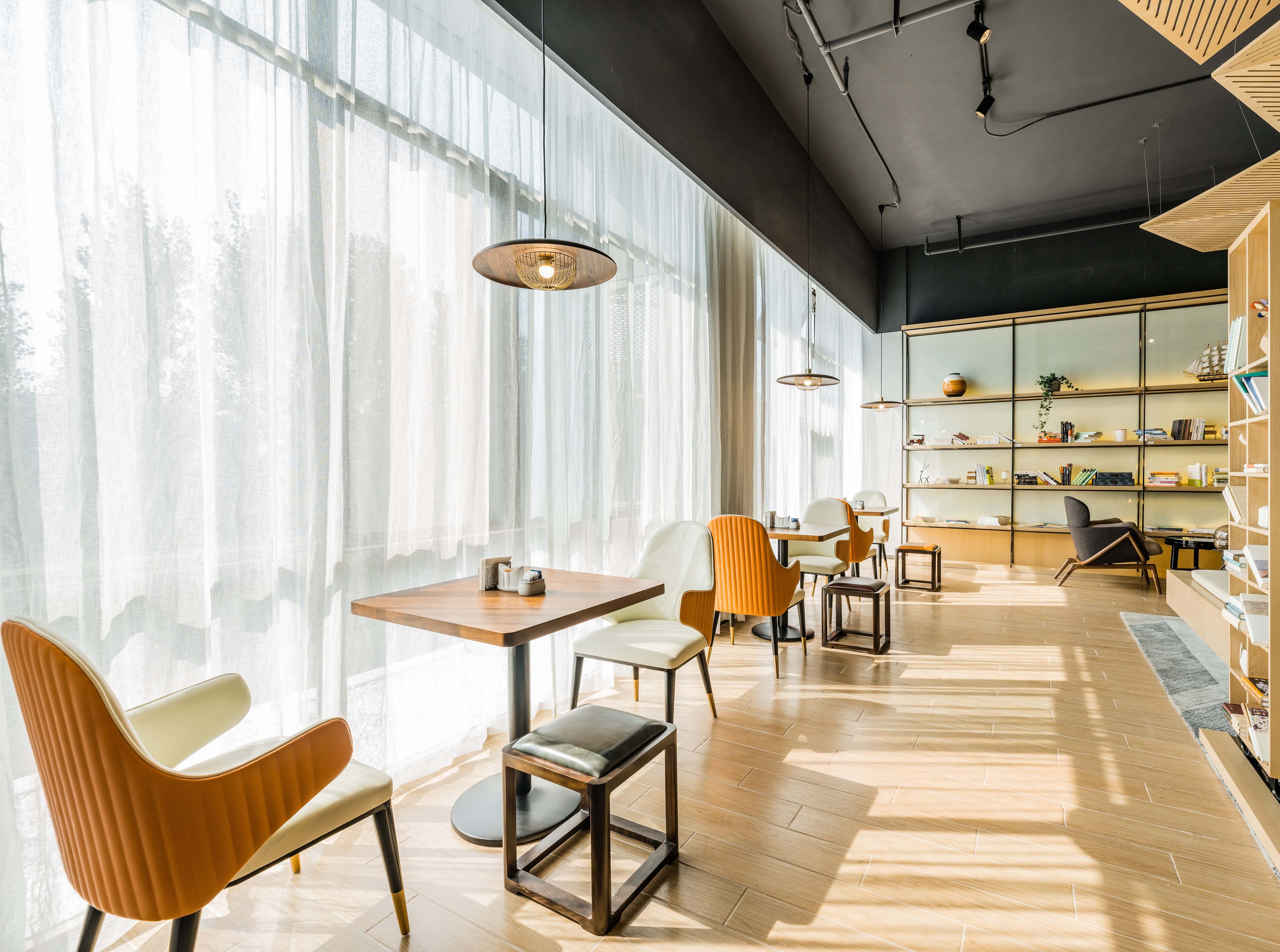 Um interior moderno com piso de madeira, uma sala de jantar com cadeiras e mesa, e uma estante cheia de livros e objetos decorativos.