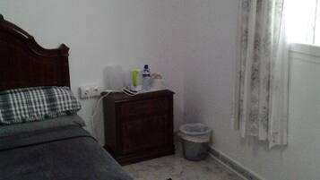 Um quarto com uma cama, uma mesa de cabeceira, uma lixeira e duas fotos emolduradas na parede.