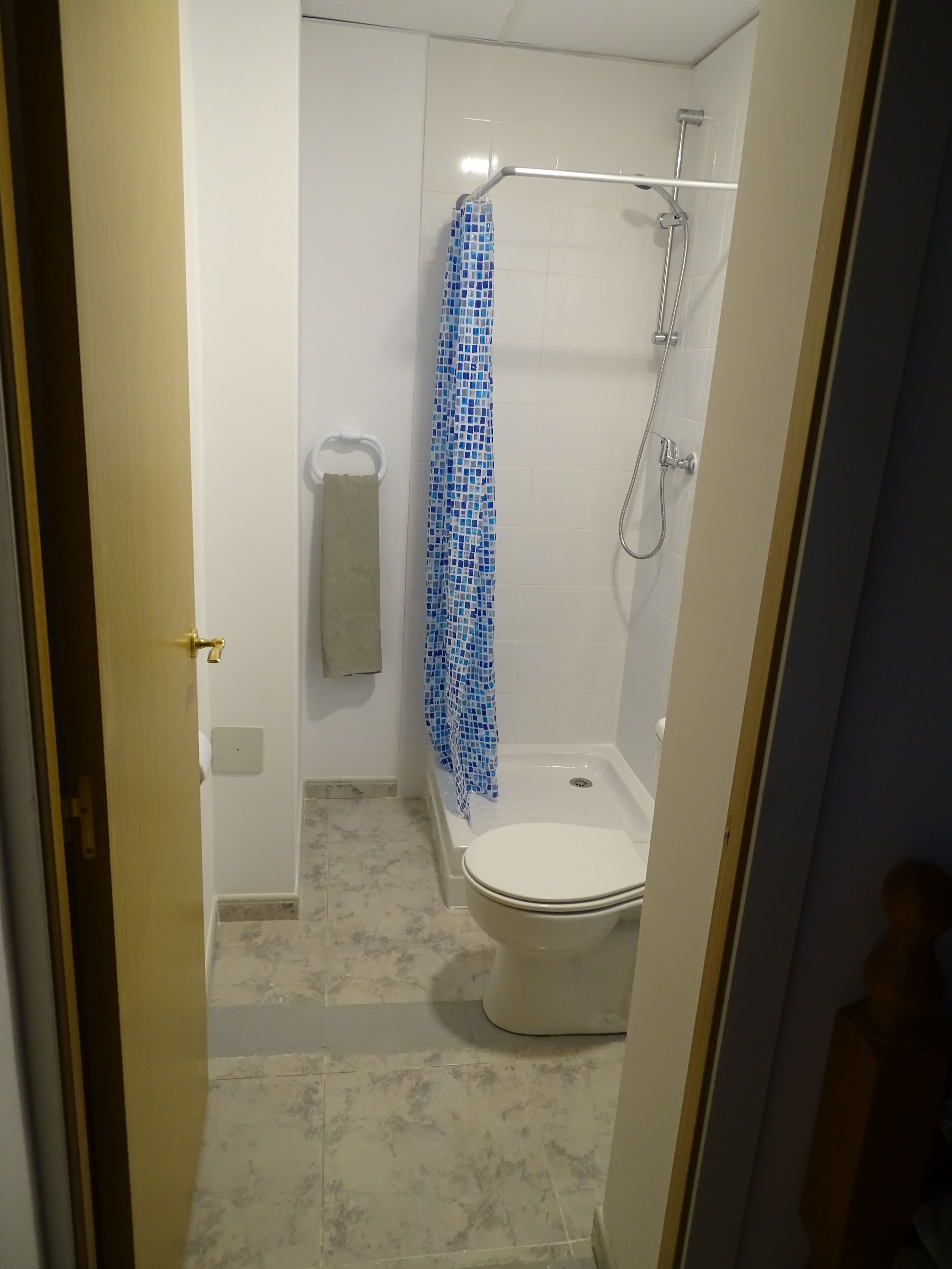 Casa de banho com sanita, chuveiro com cortina de mosaico azul e um porta-toalhas.