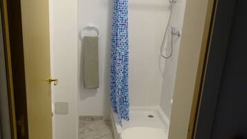 Casa de banho com sanita, chuveiro com cortina de mosaico azul e um porta-toalhas.