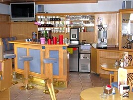 Uma área de bar com banquetas, televisão e frigorífico.