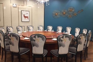 Sala de conferências com mesa redonda rodeada por cadeiras estampadas com motivos florais, um lustre e obras de arte nas paredes, incluindo uma pintura de veado e peças metálicas decorativas.