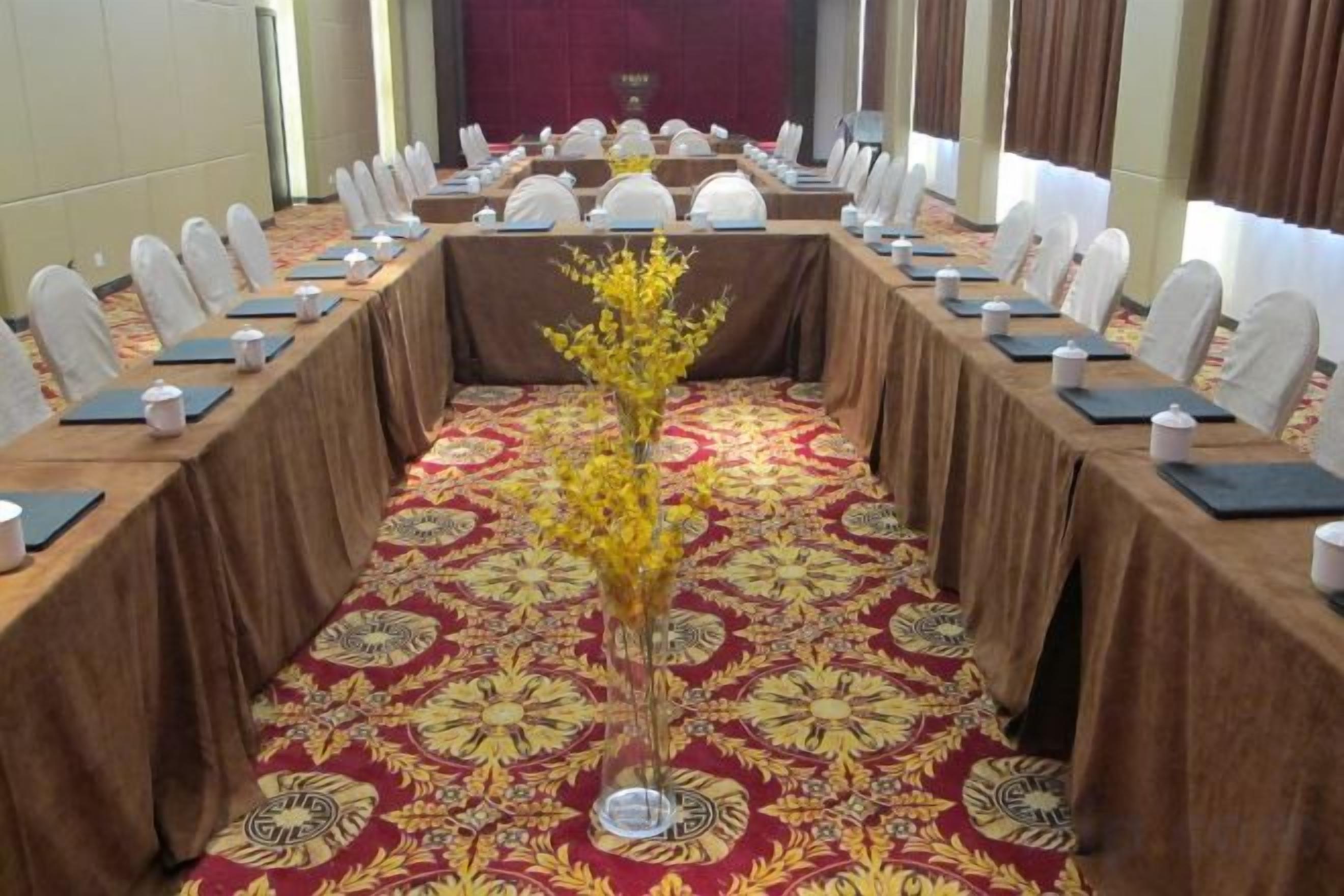 Uma sala de conferências com uma mesa comprida, cadeiras e um vaso decorativo.