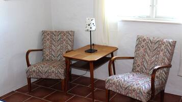 Um quarto pequeno com duas cadeiras estampadas, uma mesa de madeira e um abajur.