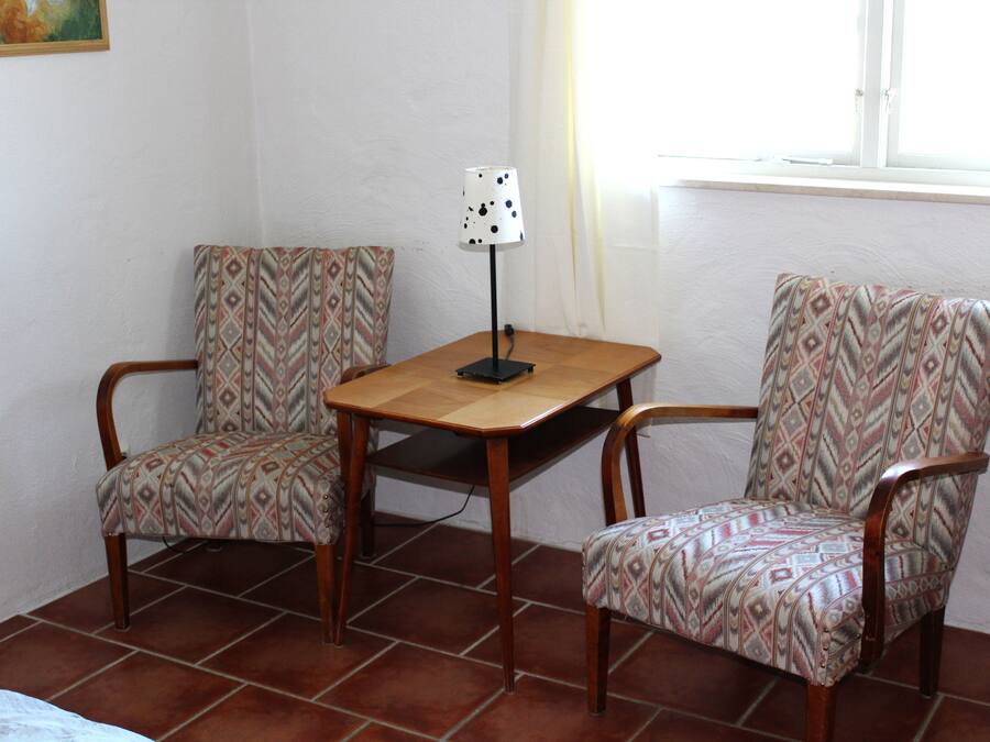 Um quarto pequeno com duas cadeiras estampadas, uma mesa de madeira e um abajur.