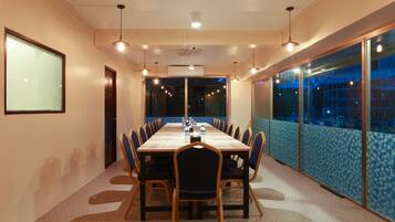 Uma sala de conferências com uma mesa comprida, cadeiras e uma janela grande com vista para a cidade à noite.