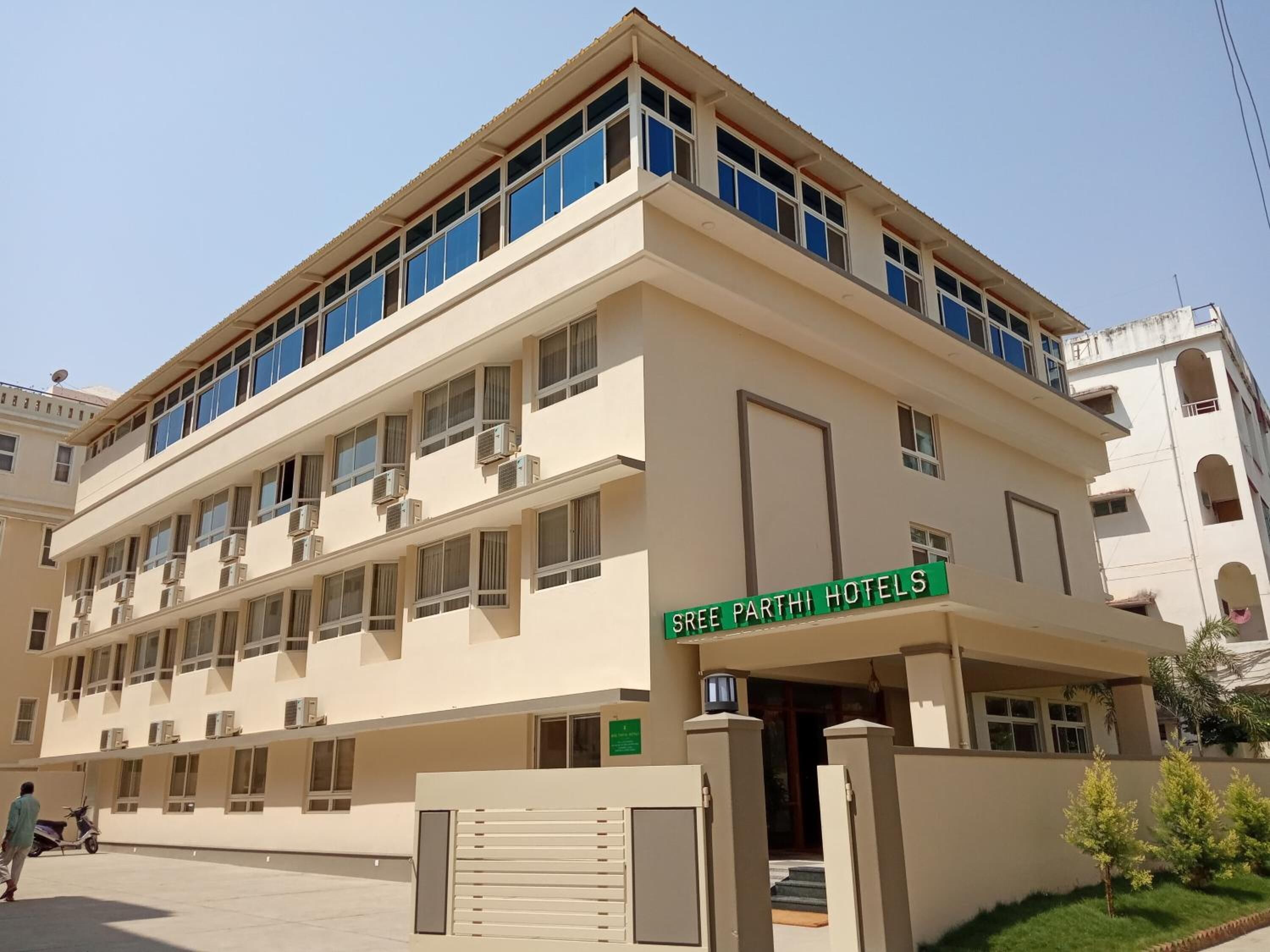 Um hotel de vários andares com fachada plana, aparelhos de ar condicionado e uma placa com a inscrição 'Sree Parthi Hotels'.