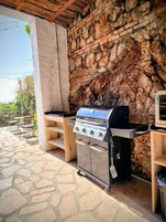 Cozinha externa com parede de pedra, churrasqueira e forno embutido.