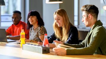 Um grupo de pessoas sentadas à mesa com laptops, um copo de suco de laranja e uma caixa de lenços.
