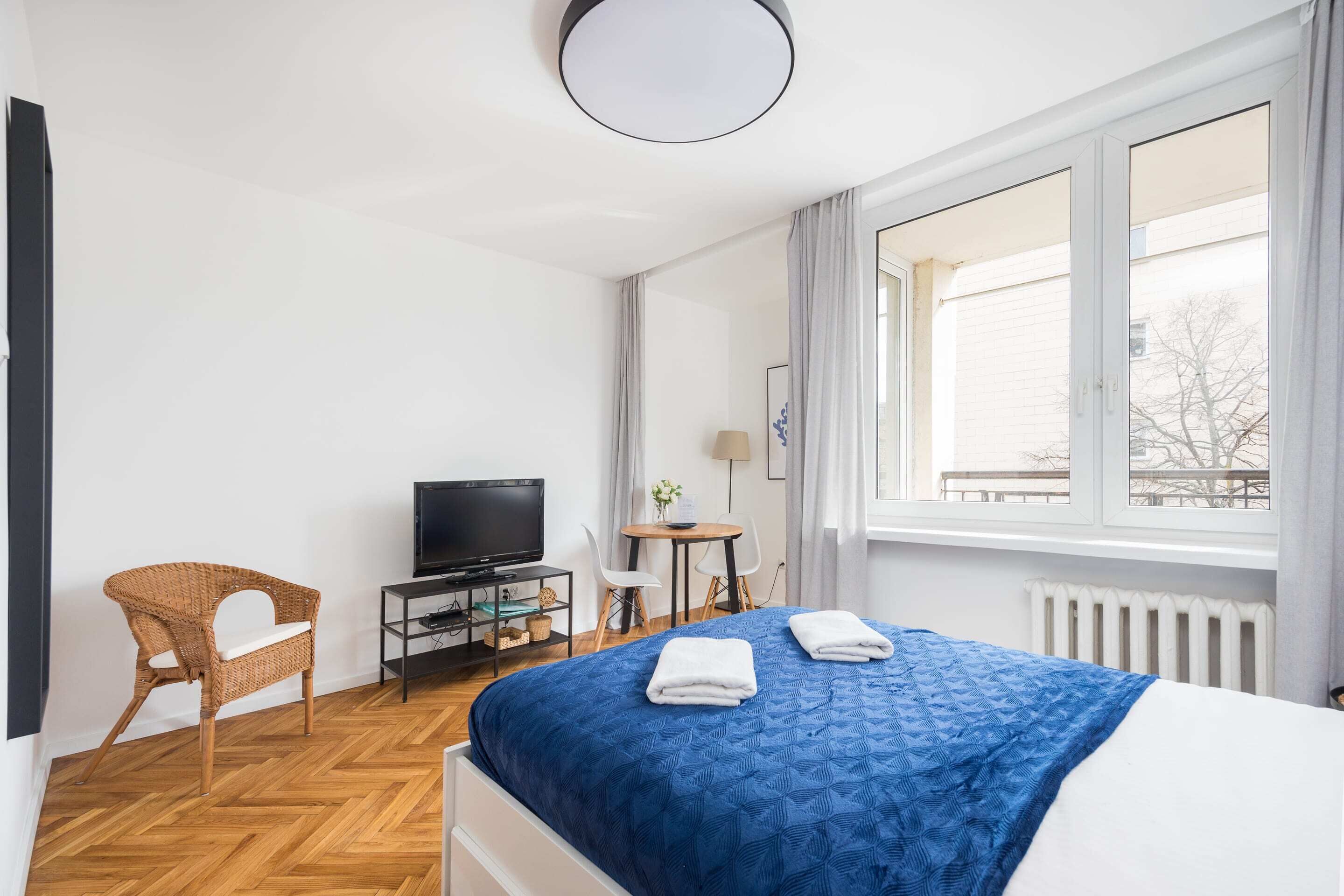 Quarto de hotel com cama, televisão, cadeira, mesa pequena e janela.