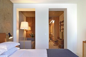 Quarto de hotel com cama, escrivaninha, luminária e cadeira.