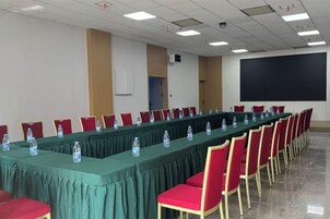 Sala de conferências com uma mesa comprida, cadeiras vermelhas e uma tela de projeção.