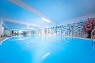 Piscina interna com água azul cristalina, rodeada por paredes com padrão floral.