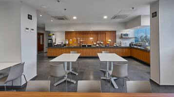 Um hall de hotel moderno com uma mesa de recepção, duas mesas brancas e cadeiras cinzentas.