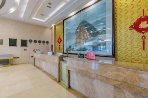 Área de recepção de hotel com balcão de mármore, uma grande obra de arte emoldurada e decoração tradicional.
