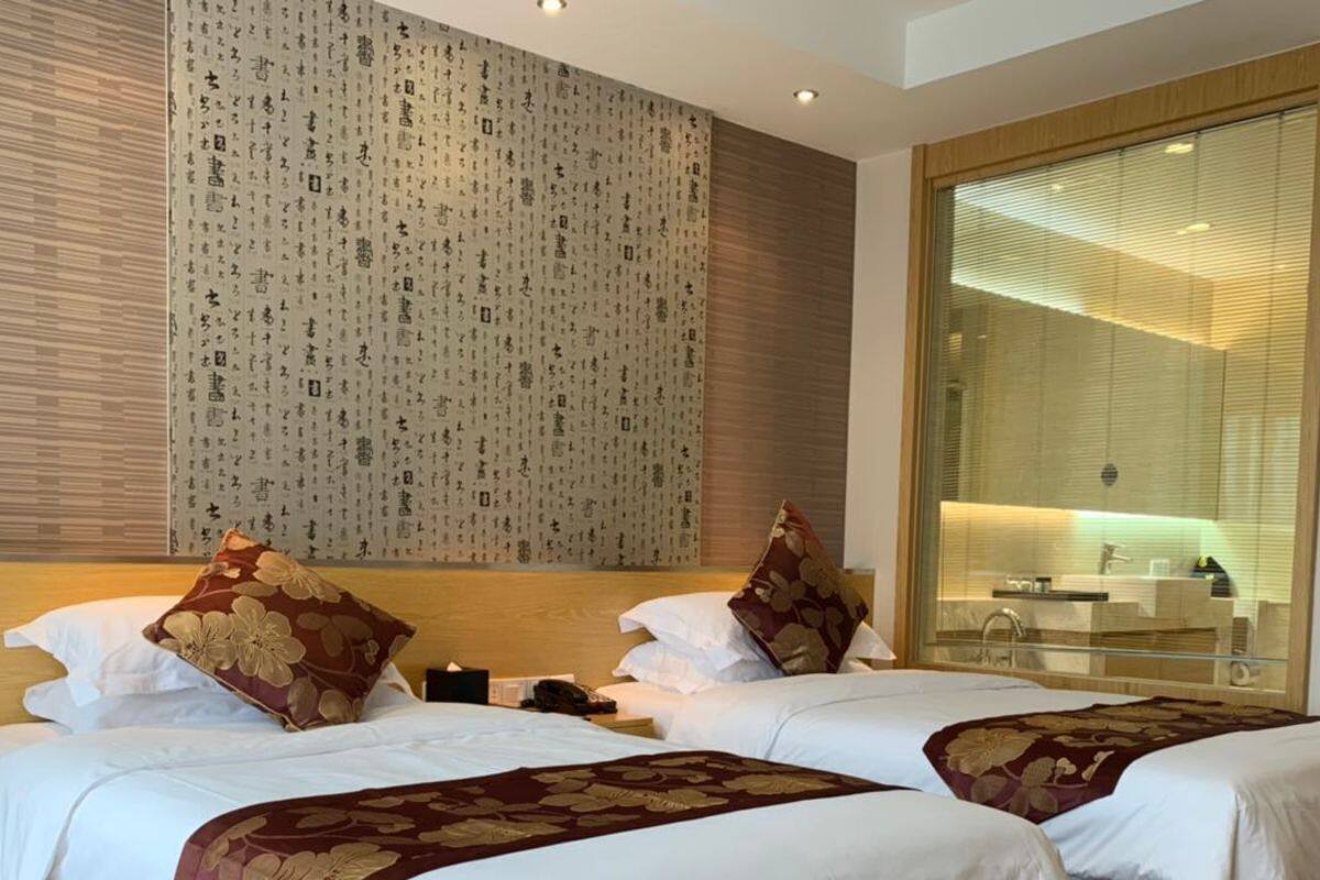 Quarto de hotel com duas camas, uma janela grande e uma parede com caligrafia.