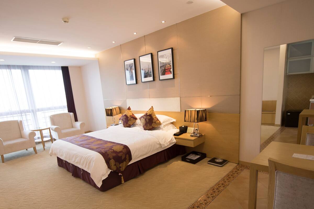 Quarto de hotel com cama grande, mesas de cabeceira, escrivaninha e uma cadeira.
