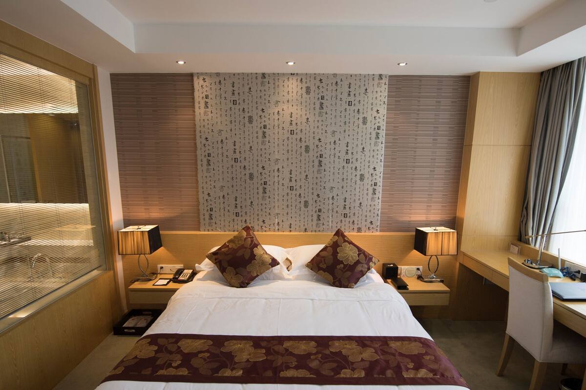 Quarto de hotel moderno com uma cama grande, duas mesas de cabeceira, uma escrivaninha e um espelho amplo.