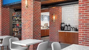 Um café moderno com paredes de tijolo, mesas de mármore branco e uma máquina de café à vista.