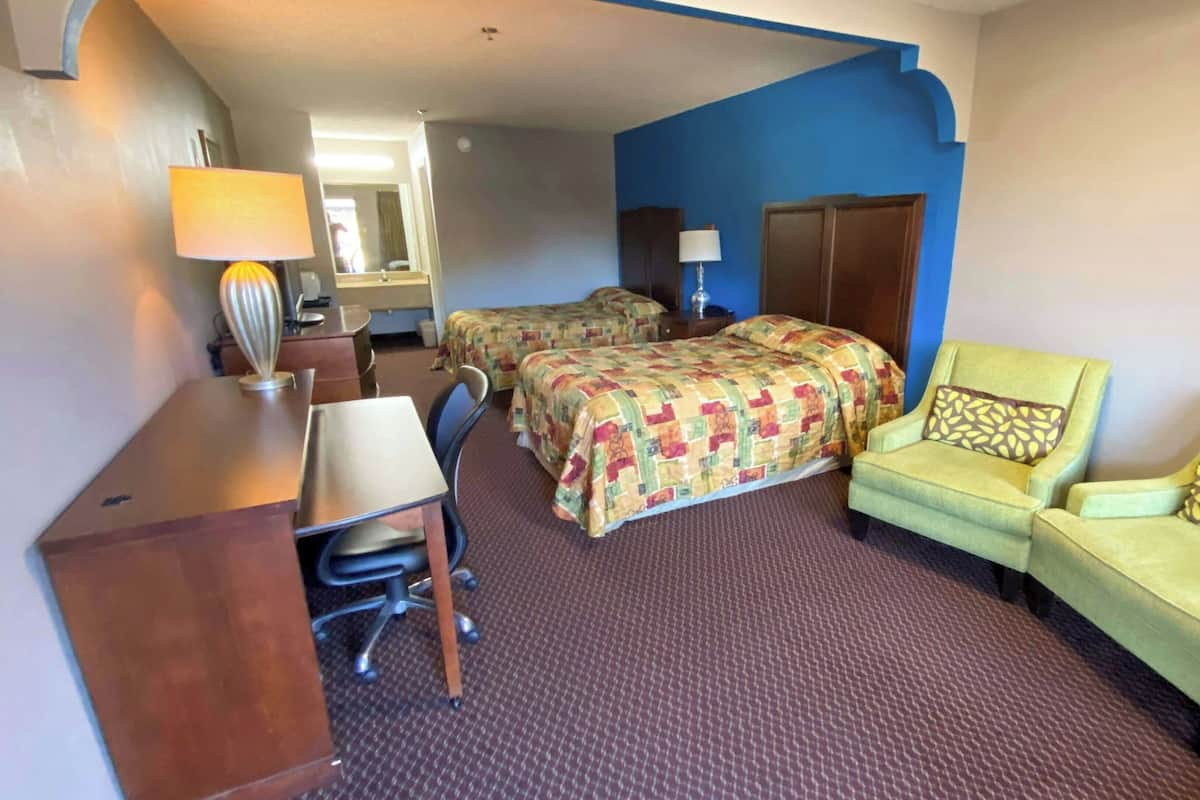Quarto de hotel com duas camas, uma escrivaninha, uma cadeira e um abajur.