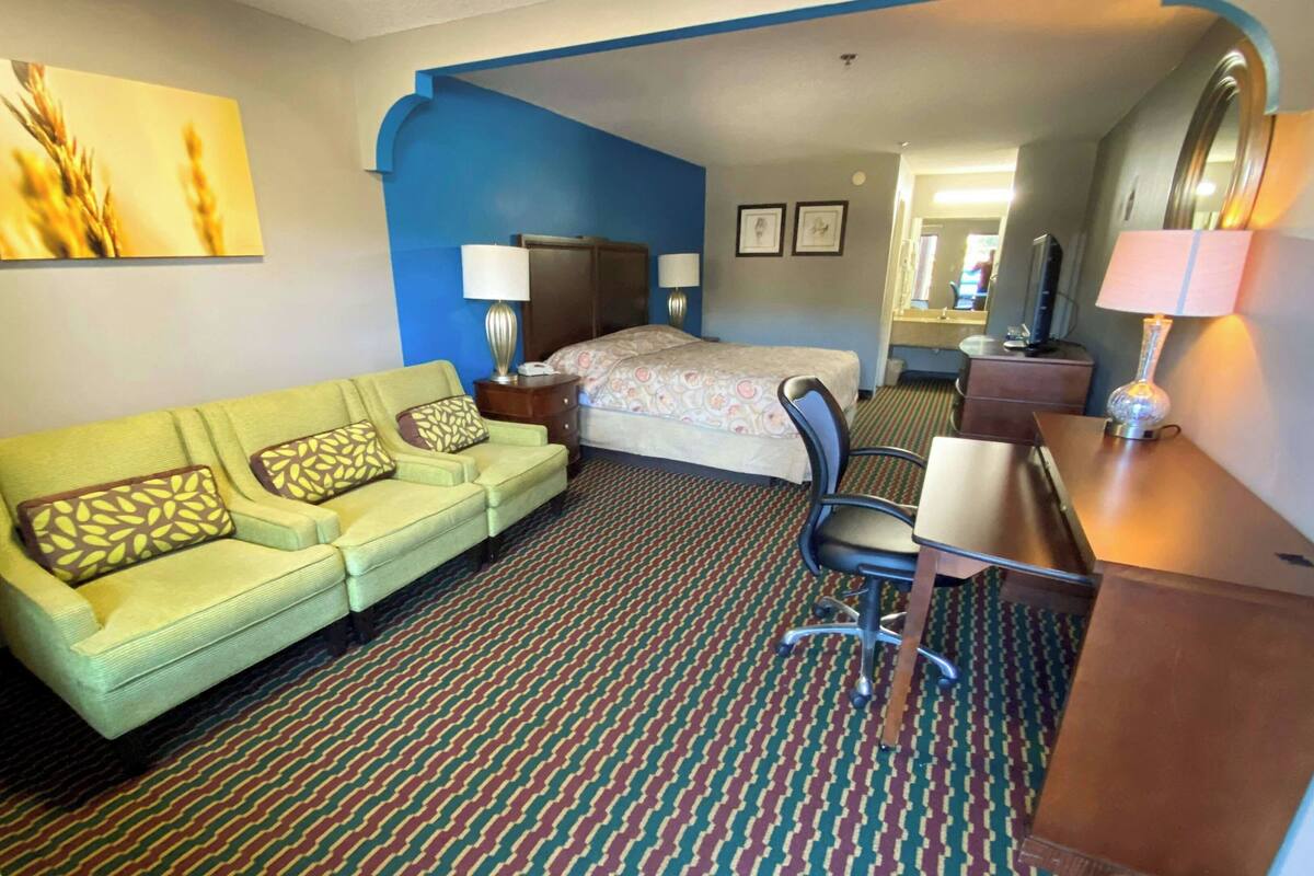 Quarto de hotel com sofá verde, uma cama, escrivaninha e espelho.