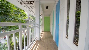 Um corredor com piso de madeira, grades brancas e uma porta verde no final.