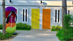 Um edifício com três portas em amarelo, laranja e roxo, e uma escultura colorida com a inscrição 'LAZY HOSTEL' em frente.