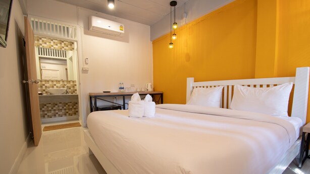 Quarto de hotel com uma cama grande, uma mesa de cabeceira, um espelho e um banheiro visível por uma porta aberta.