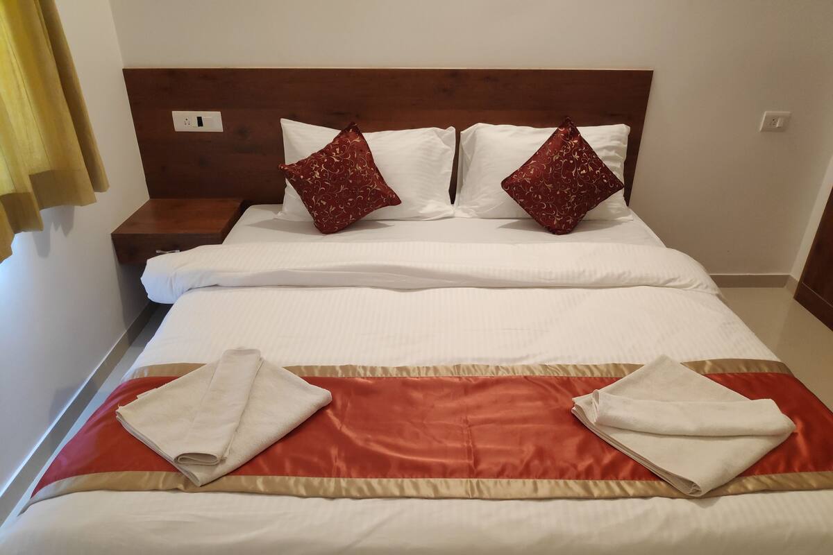 Cama bem arrumada com roupa de cama branca e vermelha, dois travesseiros decorativos e toalhas dobradas na cama.