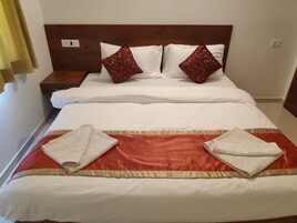 Cama bem arrumada com roupa de cama branca e vermelha, dois travesseiros decorativos e toalhas dobradas na cama.