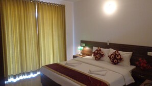 Quarto de hotel com uma cama grande, mesa de cabeceira com abajur e ventilador de teto.