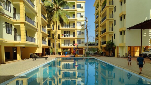 Piscina rodeada por edifícios amarelos de vários andares com varandas, uma palmeira e céu claro.
