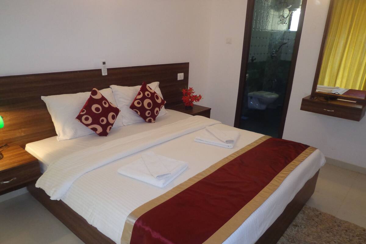 Cama bem arrumada com roupa de cama branca e vermelha, duas almofadas com estampas circulares e um cobertor vermelho.