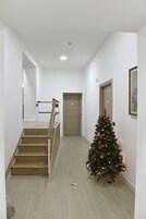 Uma escadaria que leva a uma porta, um pequeno pinheiro de Natal decorado e um quadro na parede.